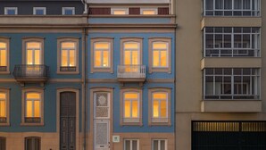 Um edifício de vários andares com fachada azul, várias janelas com iluminação quente e um portão preto na entrada.