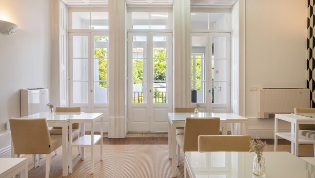 Um quarto claro e arejado, com grandes janelas, uma mesa de jantar e cadeiras.