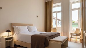 Quarto de hotel com cama, mesas de cabeceira, um banco e uma cadeira.