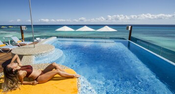 Uma área de piscina com vista clara para o oceano, espreguiçadeiras e guarda-sóis.