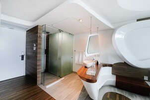 Uma casa de banho moderna com cabine de duche em vidro, lavatório branco e toucador de madeira.