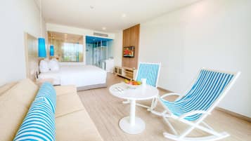 Quarto de hotel moderno com cama, sofá, mesa de jantar com frutas e televisão.