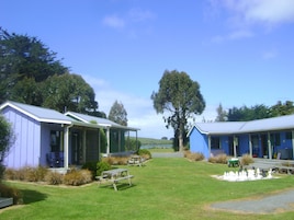 Um camping com duas cabanas azuis, mesas para piquenique e um tabuleiro de xadrez no centro.