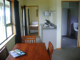 Quarto compacto com uma mesa de jantar de madeira, uma cadeira, pequeno espaço de cozinha com micro-ondas e banheiro separado.