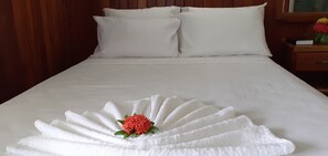Cama bem arrumada com lençóis brancos e arranjo de toalhas com um centro de flores.
