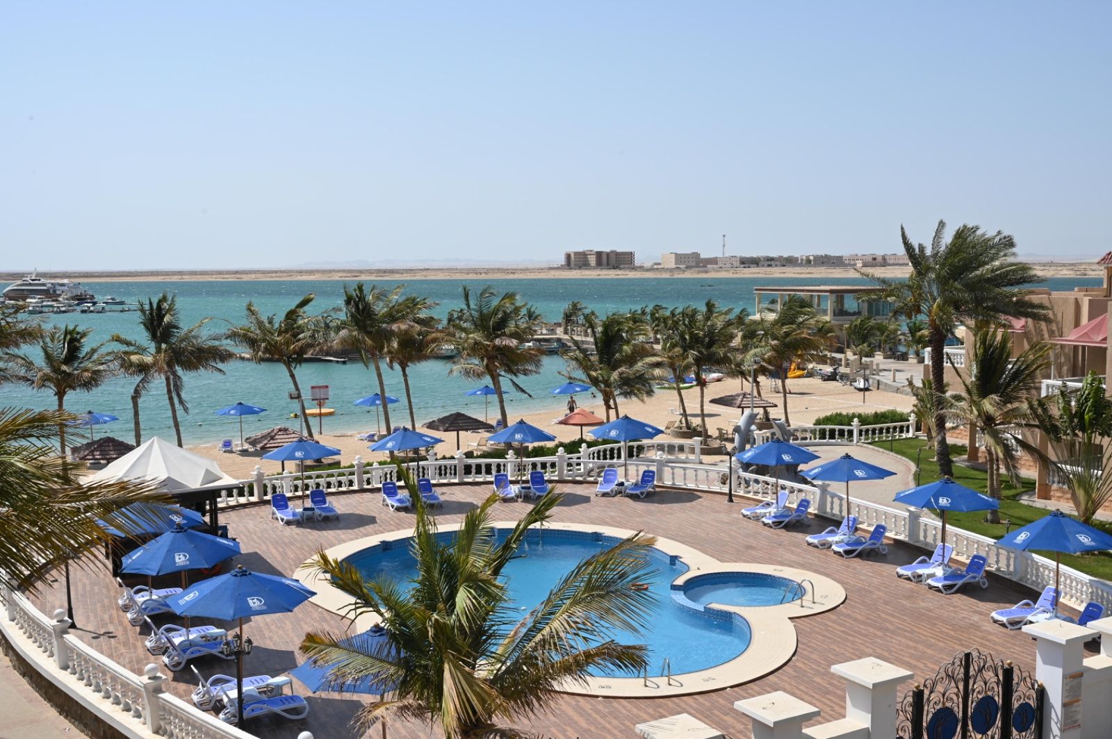 Área de piscina de resort com espreguiçadeiras e guarda-sóis, com vista para uma praia e oceano.