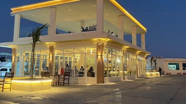 Um hotel moderno com fachada de vidro, área de estar externa e piscina.
