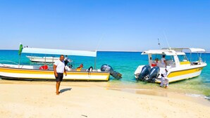 Uma praia com dois barcos atracados, areal arenoso e céu azul límpido.