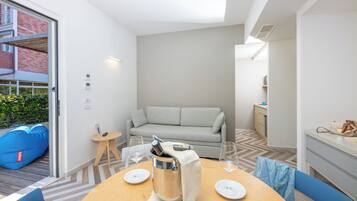Uma sala de estar moderna com uma mesa de jantar de madeira, um sofá cinzento e uma pequena mesa lateral com um controle remoto.
