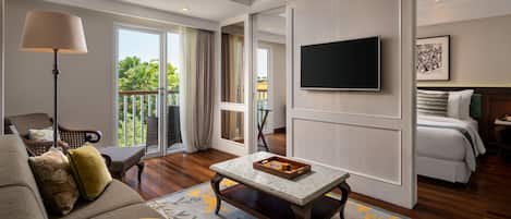 Quarto de hotel com sofá, poltrona, TV de tela plana, mesa de jantar e varanda com cortinas.