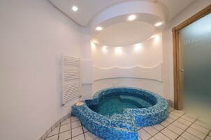Um banheiro moderno com banheira de hidromassagem em mosaico, iluminação embutida no teto e radiador branco.