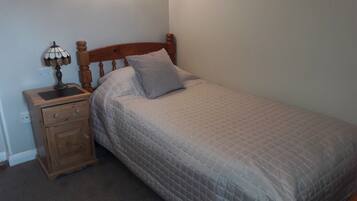 Quarto com cama de madeira, mesa de cabeceira com abajur e luminária fixada na parede.