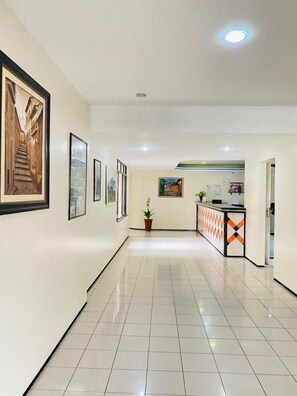 Um corredor com obras de arte emolduradas nas paredes, um balcão de recepção e piso revestido de azulejos.