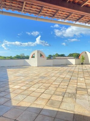 Terraço no telhado com piso de azulejos, estrutura de pérgola e céu azul claro.
