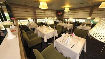 Restaurante com mesas postas para refeição, com toalhas brancas e cadeiras verdes.