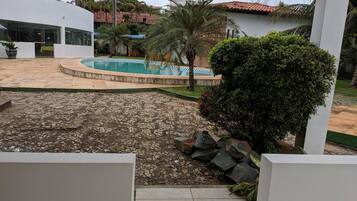 Piscina com deck revestido, cercada por palmeiras e uma pequena área de jardim.