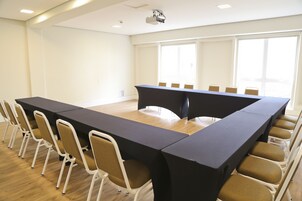Uma sala de conferências com uma mesa grande, cadeiras e um projetor.