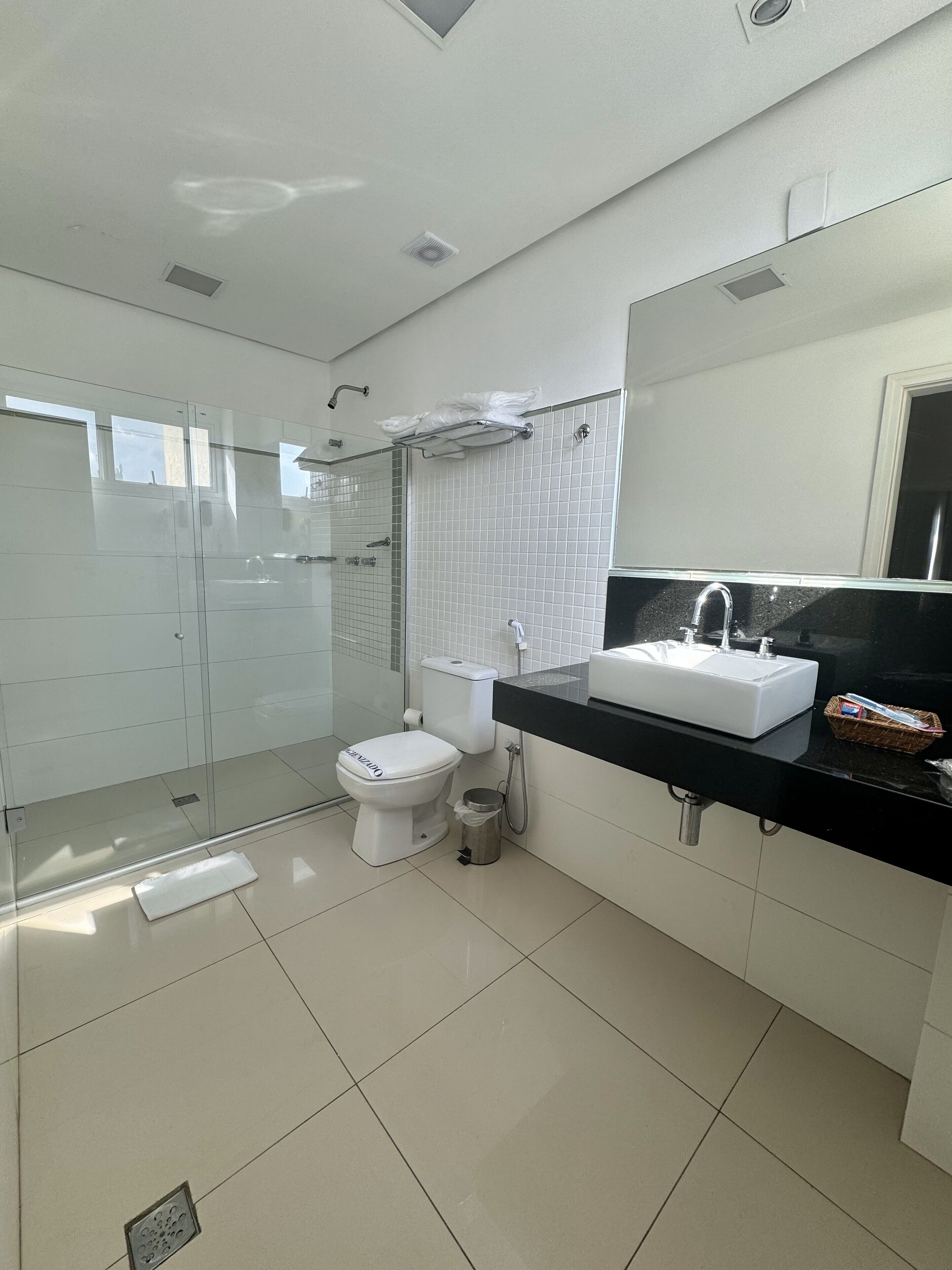 Um banheiro moderno com box de vidro, vaso sanitário branco e bancada preta com pia.