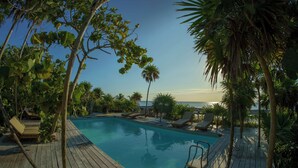 Um deck de madeira com piscina, espreguiçadeiras e palmeiras.