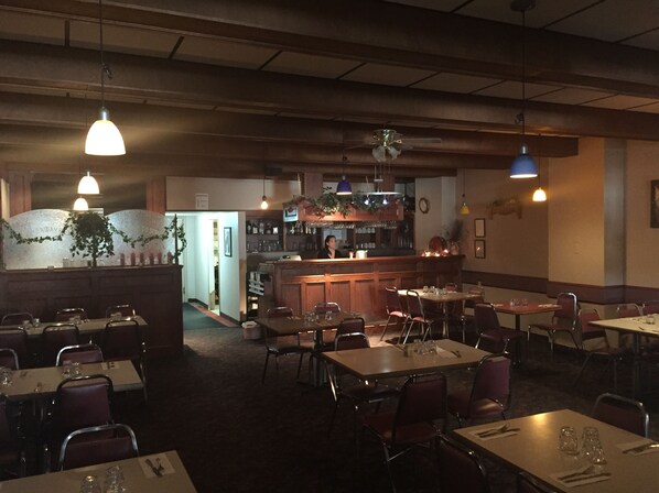 Um restaurante com mesas e cadeiras de madeira, área de bar e luminárias pendentes.