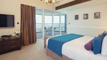 Quarto de hotel com cama grande, televisão de tela plana, escrivaninha com gavetas, cadeira, varanda com vista para a cidade e lustre.