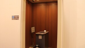 Um elevador com paredes de madeira, uma lixeira e uma placa indicando o horário de funcionamento.
