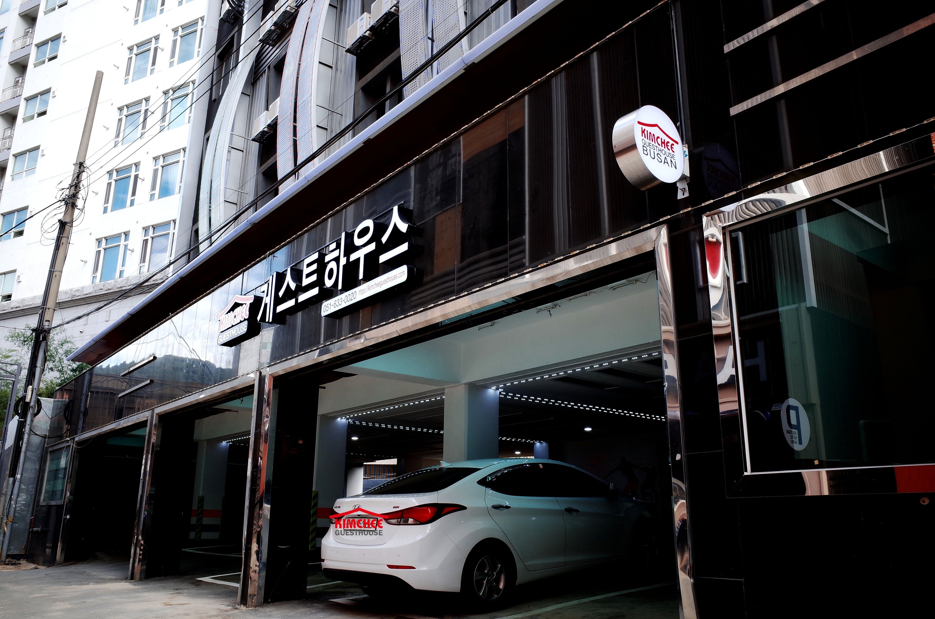 Um edifício com uma placa que diz "Kimchi Guesthouse" e um carro branco estacionado na frente.