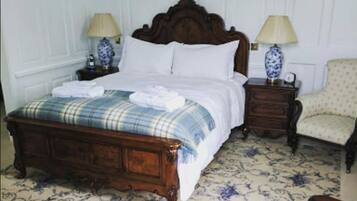 Quarto tradicional com cama de madeira, mesa de cabeceira combinando, uma cadeira e piso estampado.