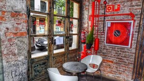 Um café rústico com paredes de tijolo aparente, uma porta de madeira antiga e um extintor de incêndio vermelho fixado na parede.