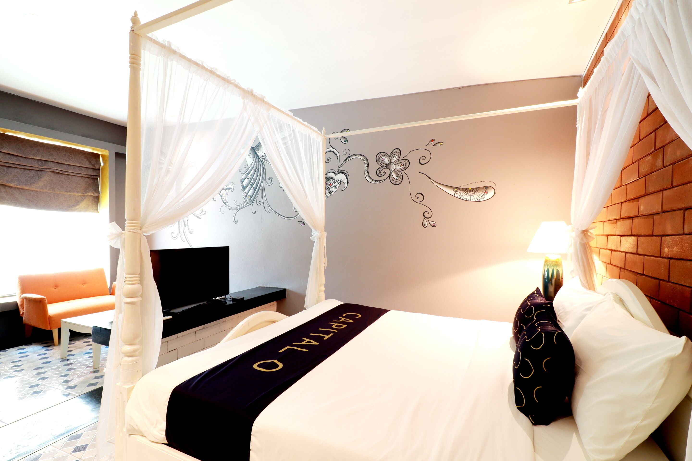 Quarto de hotel com cama de dossel, televisão de tela plana, sofá e um mural decorativo na parede.
