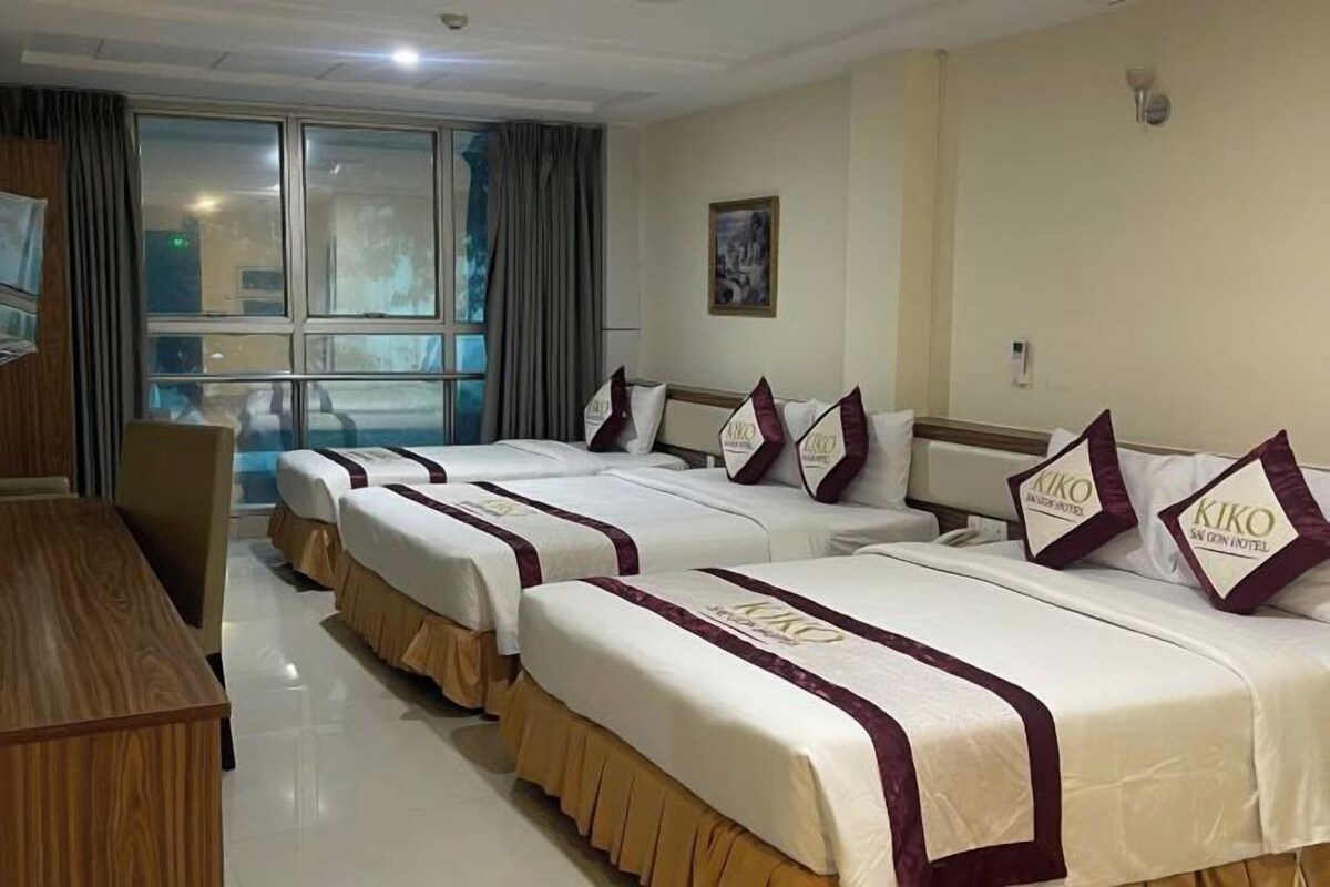 Quarto de hotel com quatro camas, cada uma com cabeceira e almofadas com a etiqueta "KIKO".