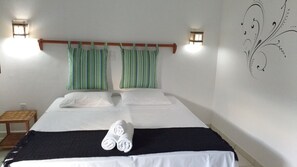 Cama bem arrumada com lençóis brancos, um espalhador preto e duas almofadas listradas de verde. Há duas luminárias de cabeceira, uma pequena mesa de cabeceira de madeira e um objeto decorativo na parede.