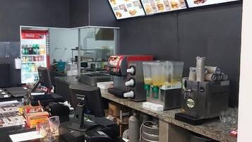 Interior de um restaurante de fast-food, com uma estação de bebidas de serviço próprio, um refrigerador de Coca-Cola e um quadro de menu exibindo os pratos.
