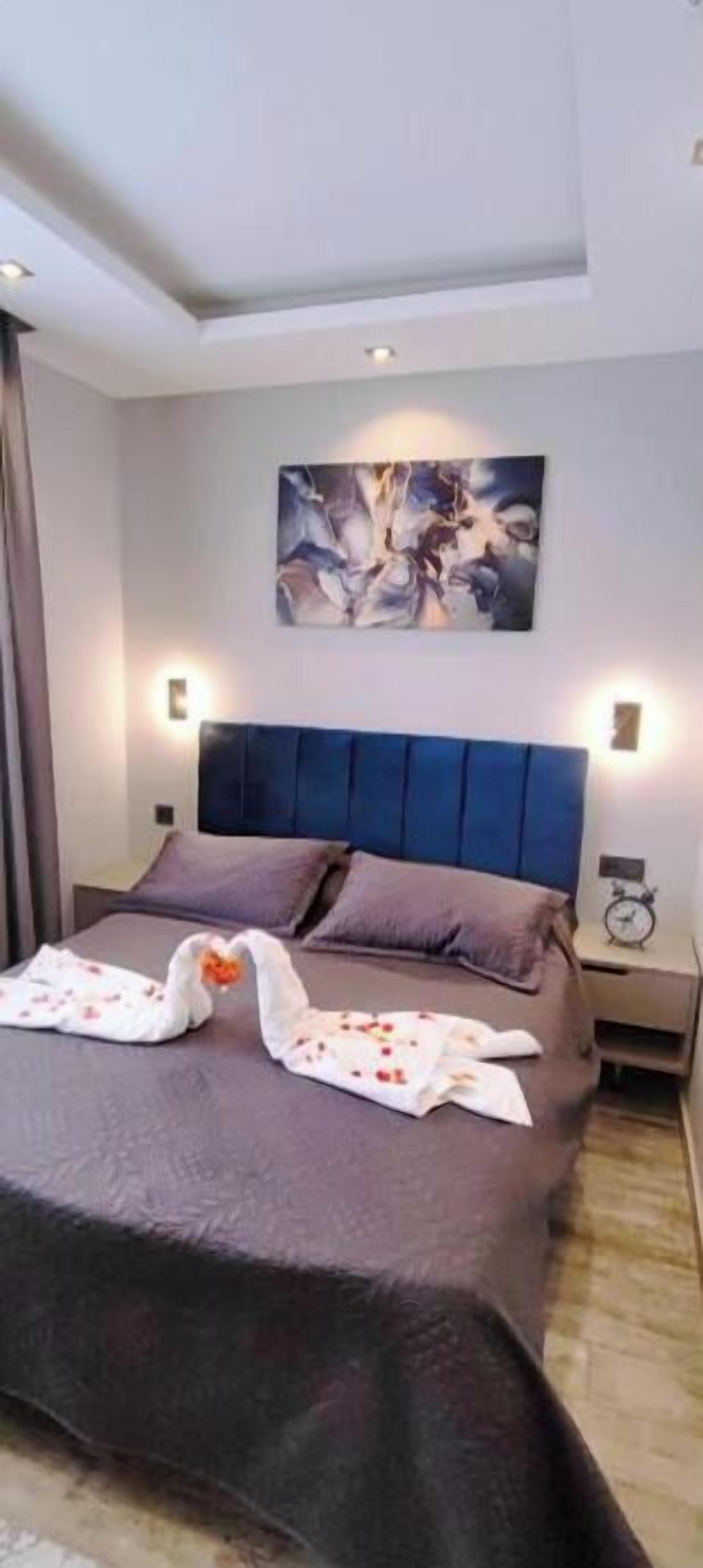 Quarto com cama, cabeceira, pintura na parede e abajures de cabeceira.