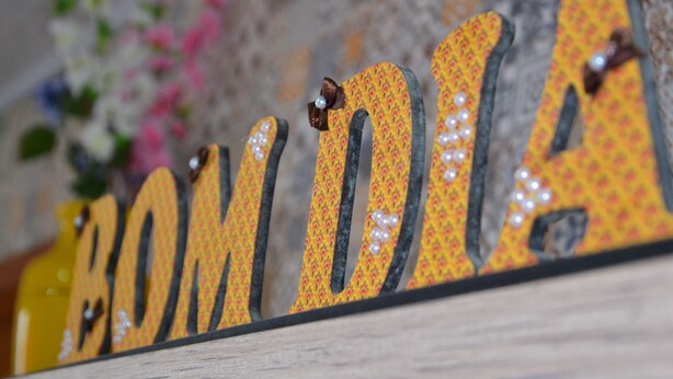 Uma placa de madeira com a palavra 'BONDA' em letras grandes, decorada com pérolas e um laço marrom.