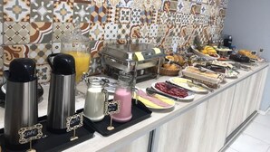 Disposição de buffet com diversos alimentos e bebidas, incluindo um canto de café e um bar de sucos.