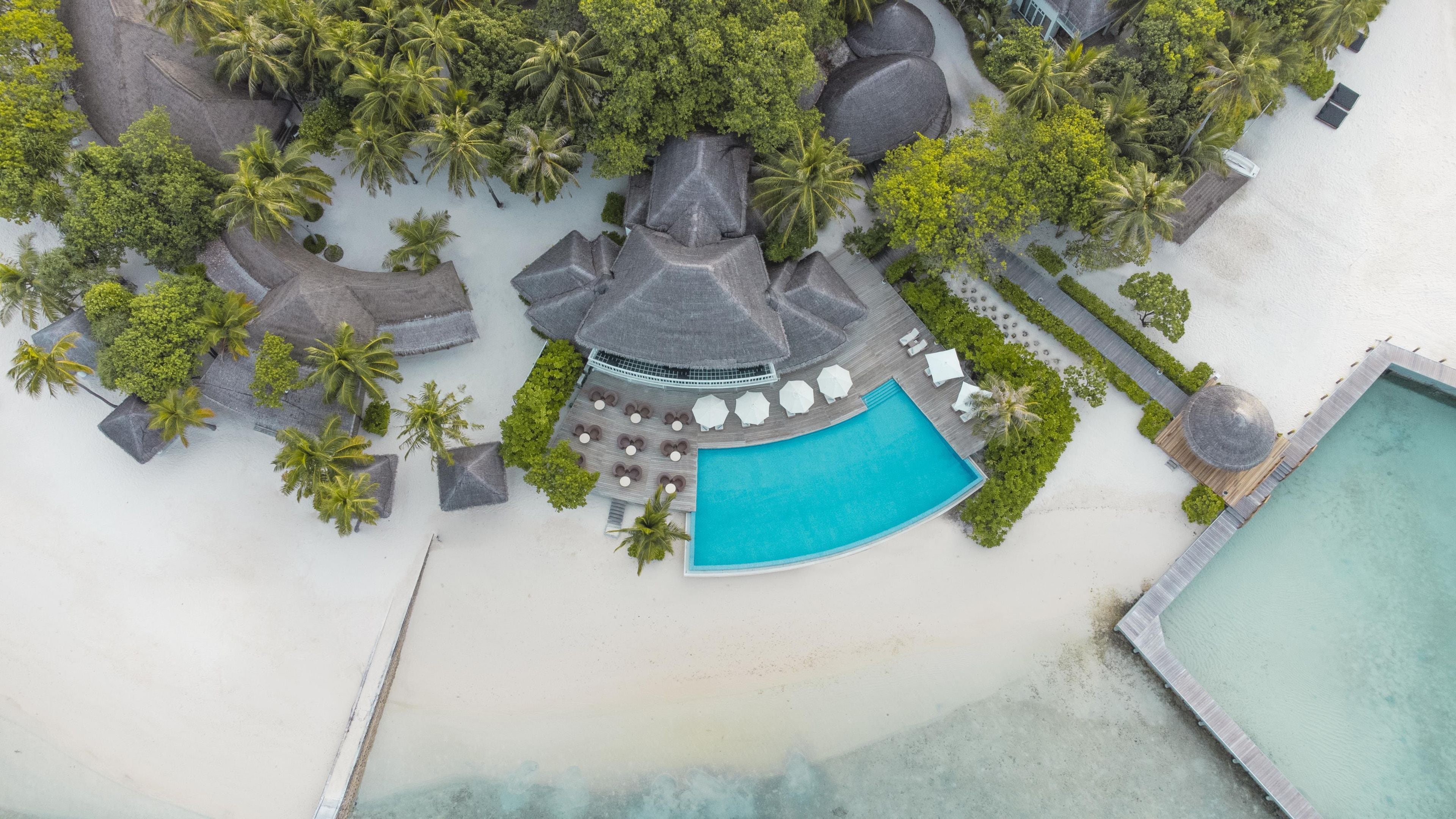 Vista aérea de um resort com piscina, palmeiras e praia.