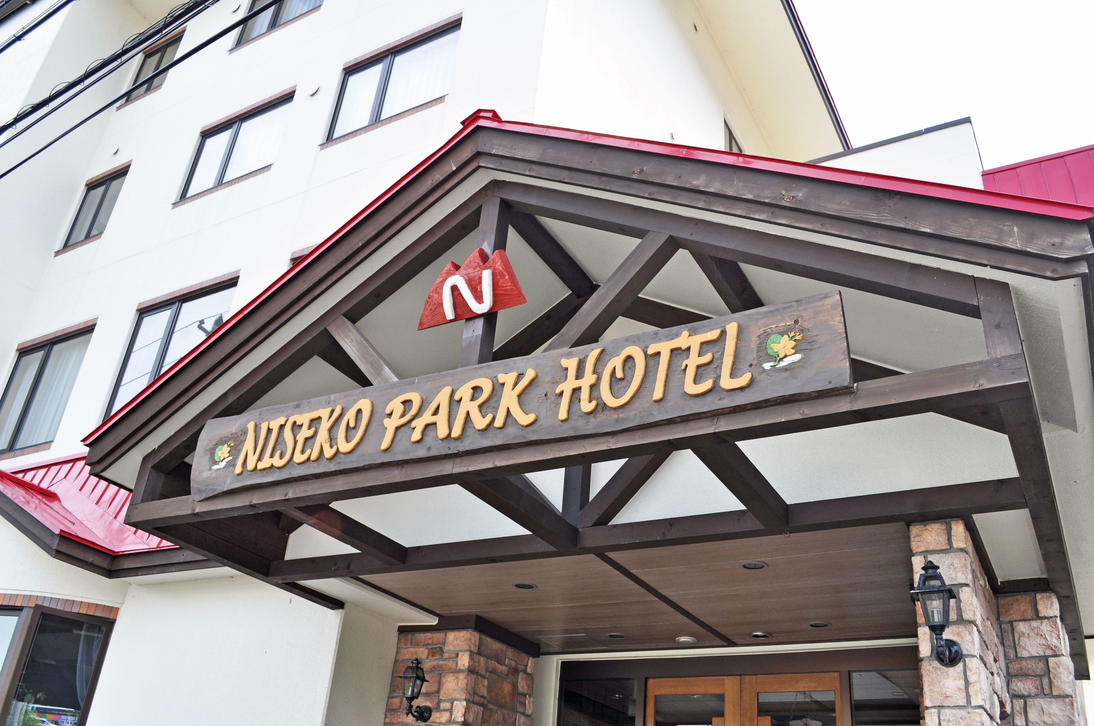 Exterior do Niseko Park Hotel, com uma placa visível, telhado vermelho e fachada de pedra.
