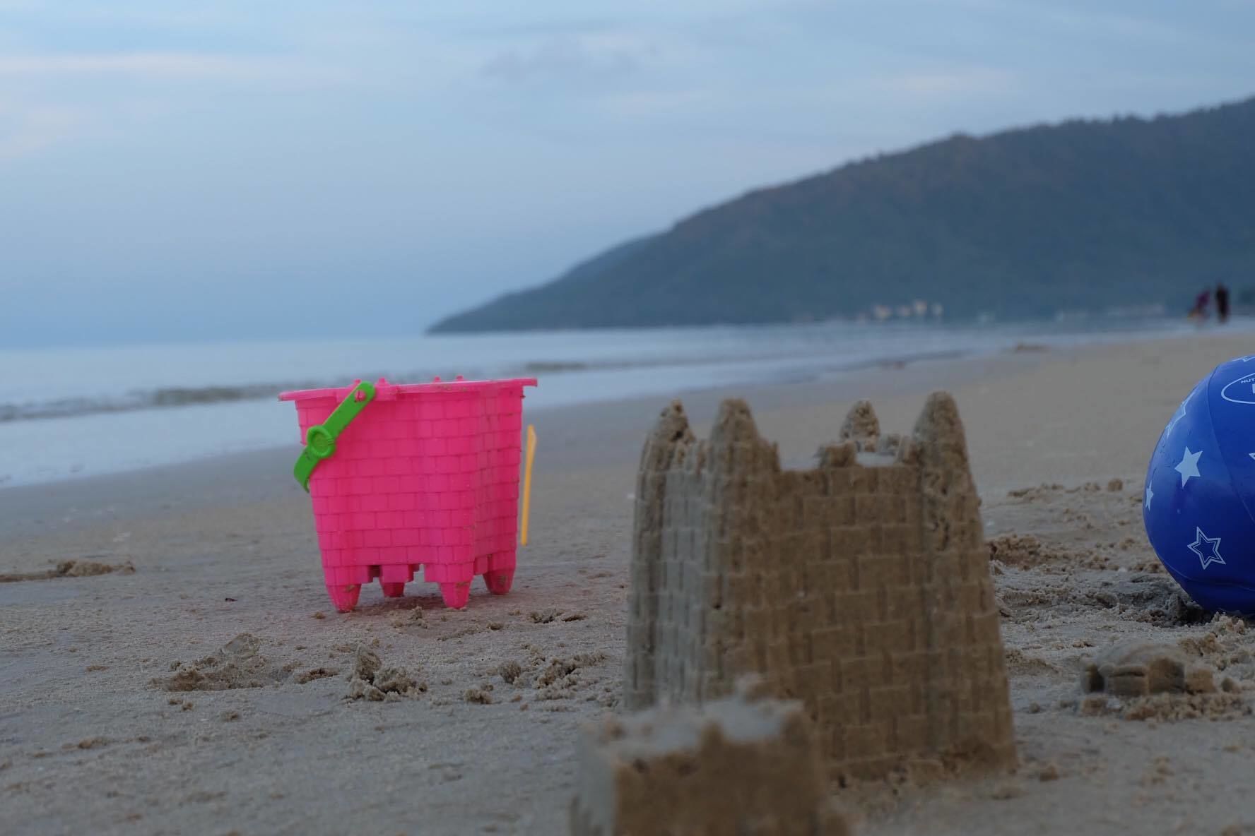Uma praia com um castelo de areia rosa e uma bola azul com estrelas.