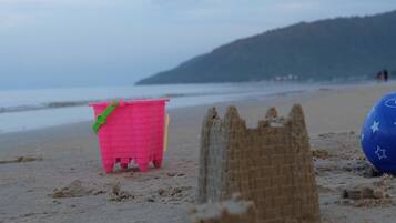 Uma praia com um castelo de areia rosa e uma bola azul com estrelas.