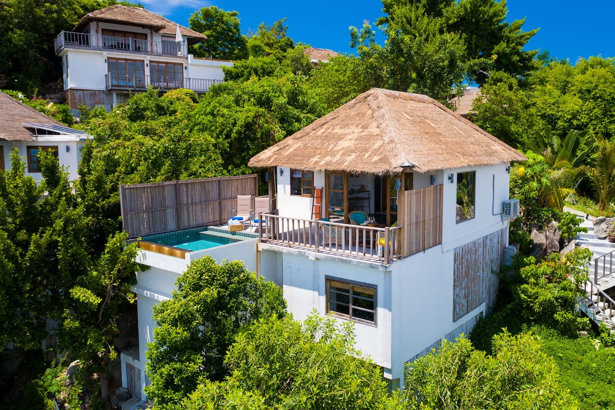 Um edifício branco com telhado de palha, varanda e piscina.