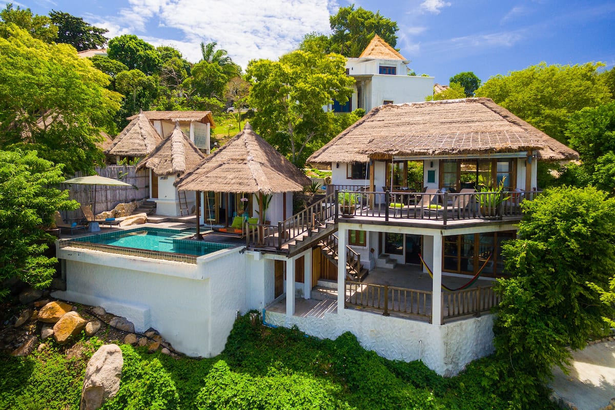 Resort com várias estruturas de telhado de palha, piscina e vegetação exuberante.