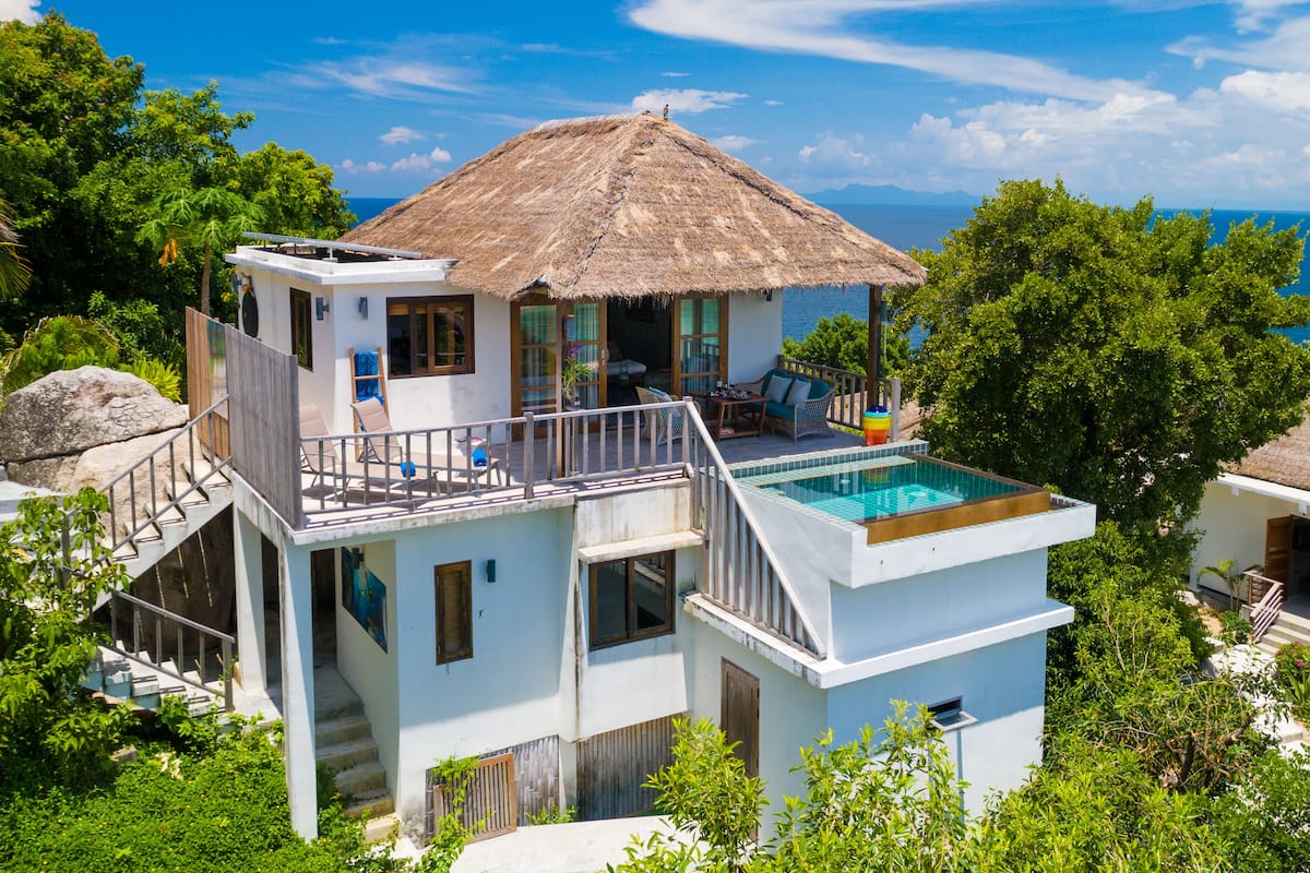 Uma vila moderna com telhado de palha, piscina e vista para o mar.