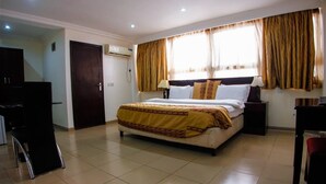 Quarto de hotel com cama, escrivaninha, cadeira, ar condicionado e janela com cortinas.