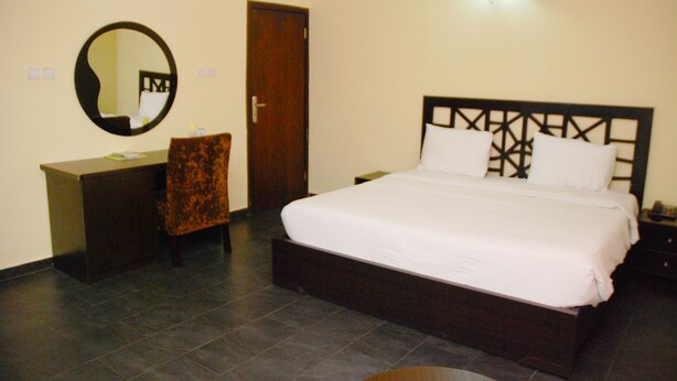 Quarto de hotel com uma cama, escrivaninha, cadeira, espelho e unidade de ar condicionado.