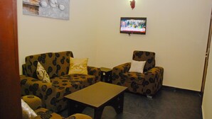 Uma sala de estar com sofás estampados, uma mesa de centro, uma televisão de tela plana e um quadro na parede.