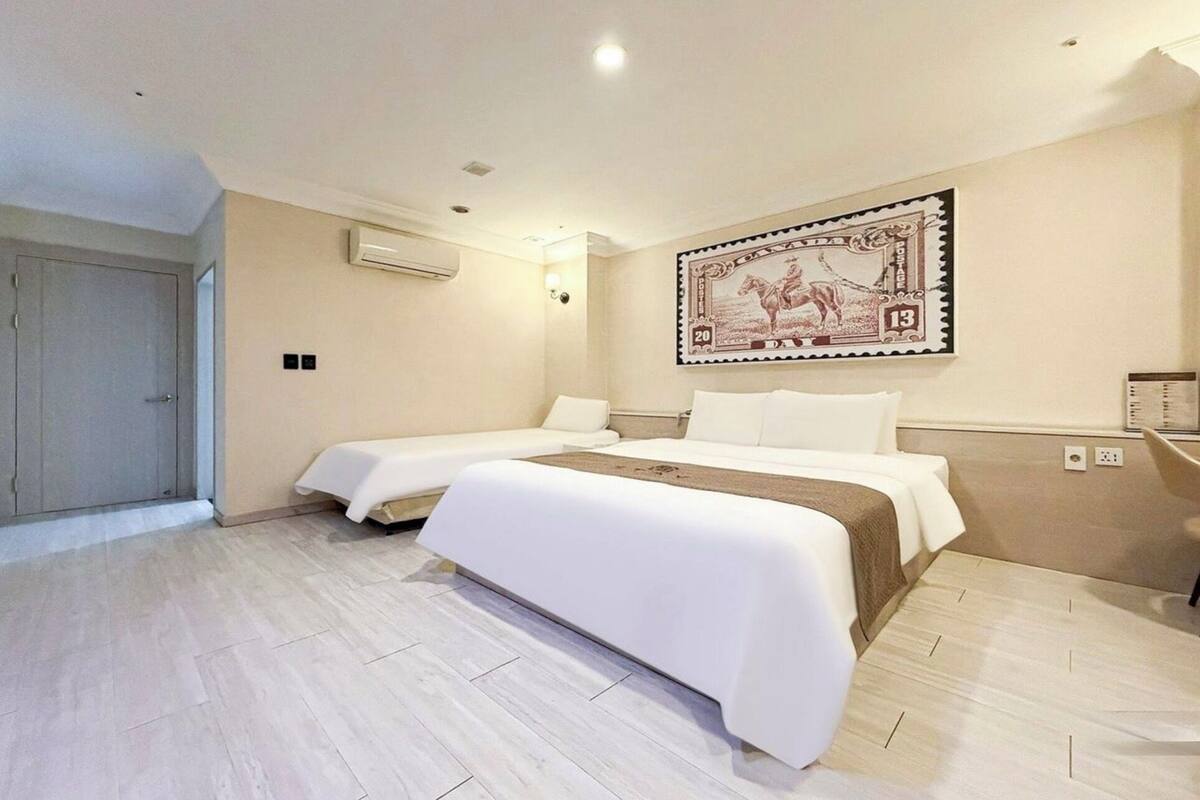 Quarto de hotel com duas camas, uma obra de arte grande pendurada na parede e piso de madeira.