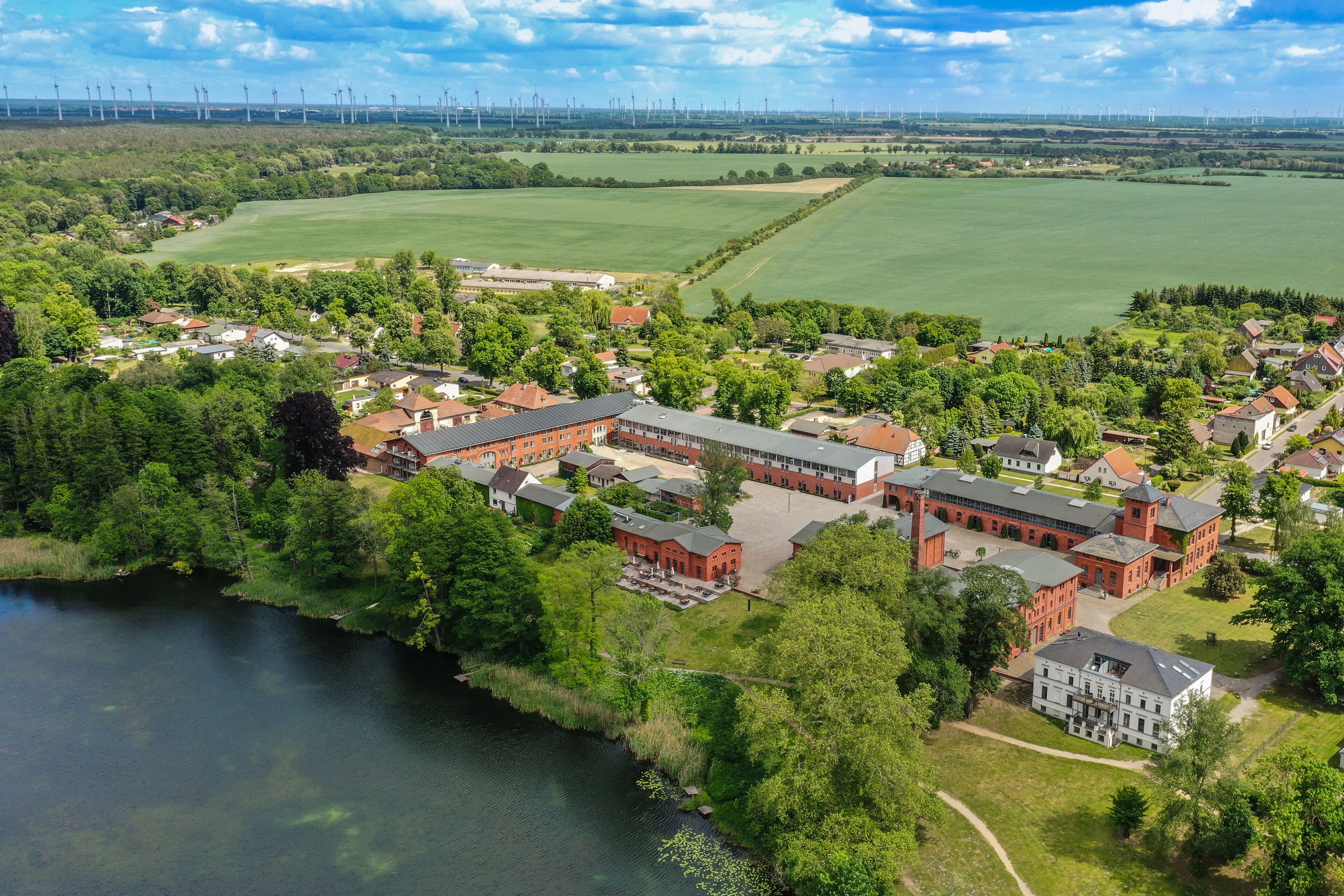 Vista aérea de um campus com vários edifícios, um rio e campos verdes ao redor.