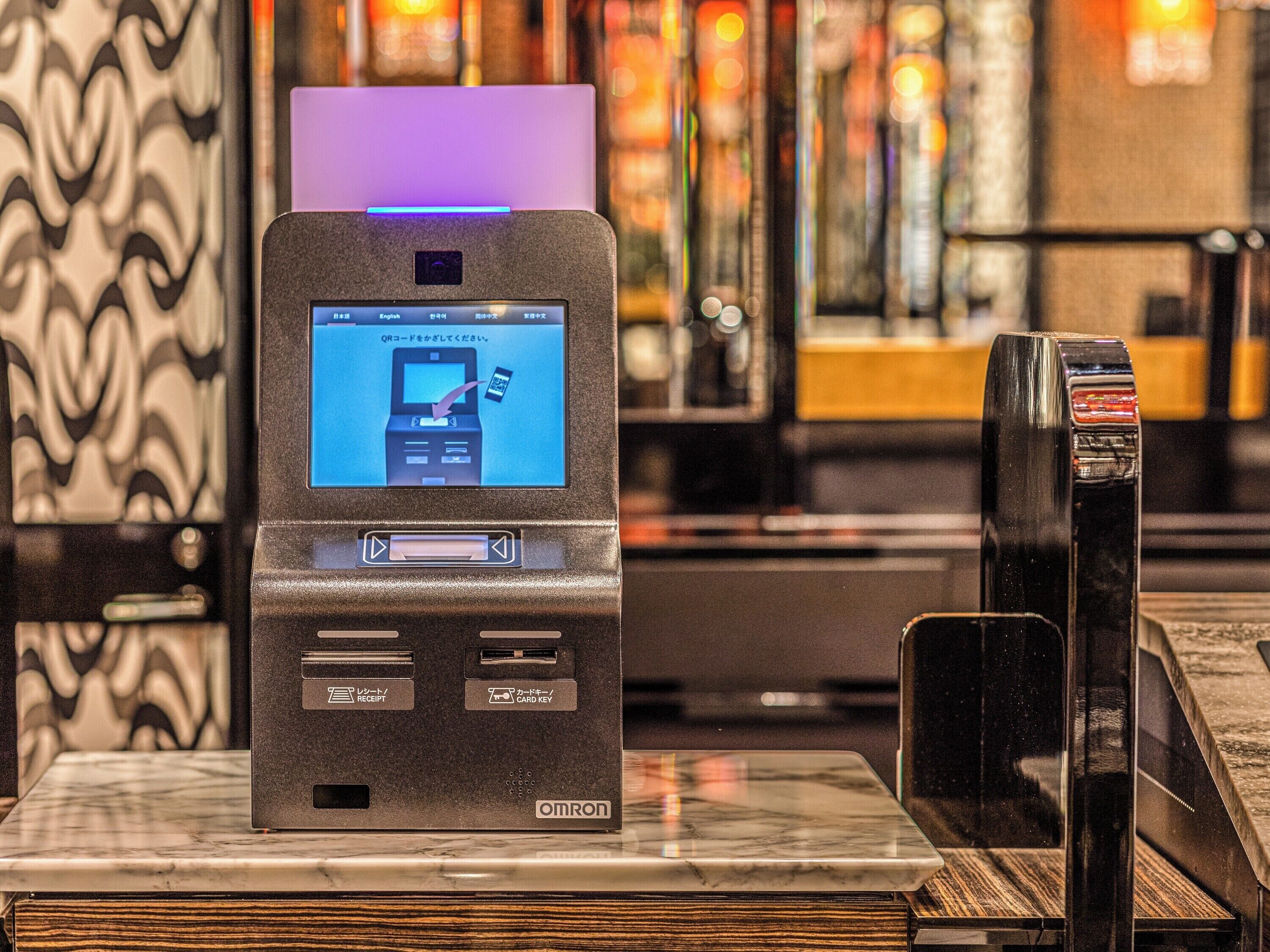 Um quiosque de autoatendimento com tela exibindo instruções para leitura de código QR, uma abertura para recibos e uma entrada para chave de cartão.