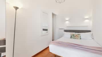 Quarto com cama, mesa de cabeceira, abajur, espelho e luminária na parede.